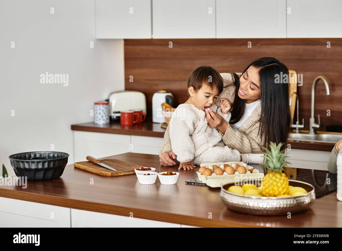 A joyful mother feeding son as cooking in modern kitchen, celebrating ...