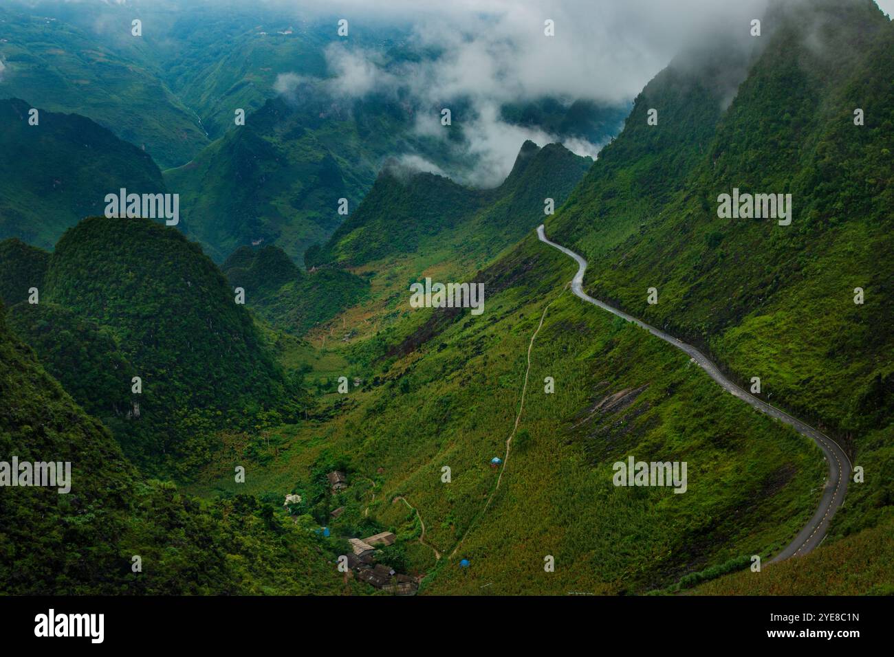Curvy mountain road cuts through the side of the lush green misty ...