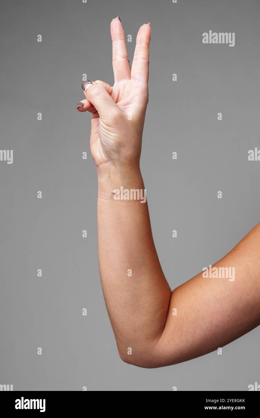 A hand gestures the peace sign against a neutral gray background Stock ...