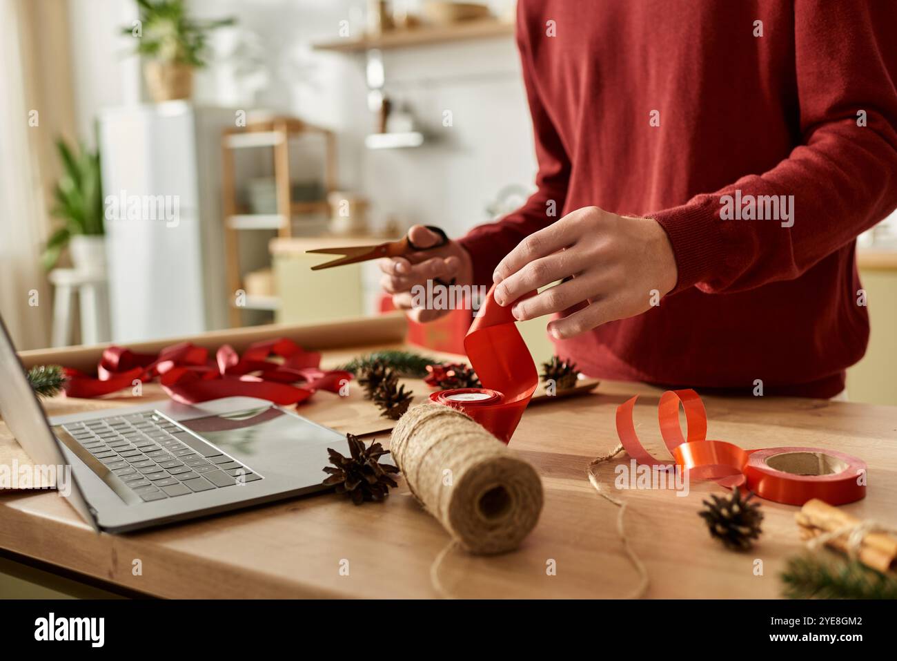 A young man wraps Christmas gifts in a warm kitchen with red ribbons ...