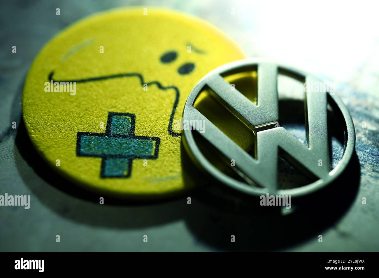 VW-Zeichen im Schatten und Emoji mit Pflaster, Symbolfoto VW-Krise ...