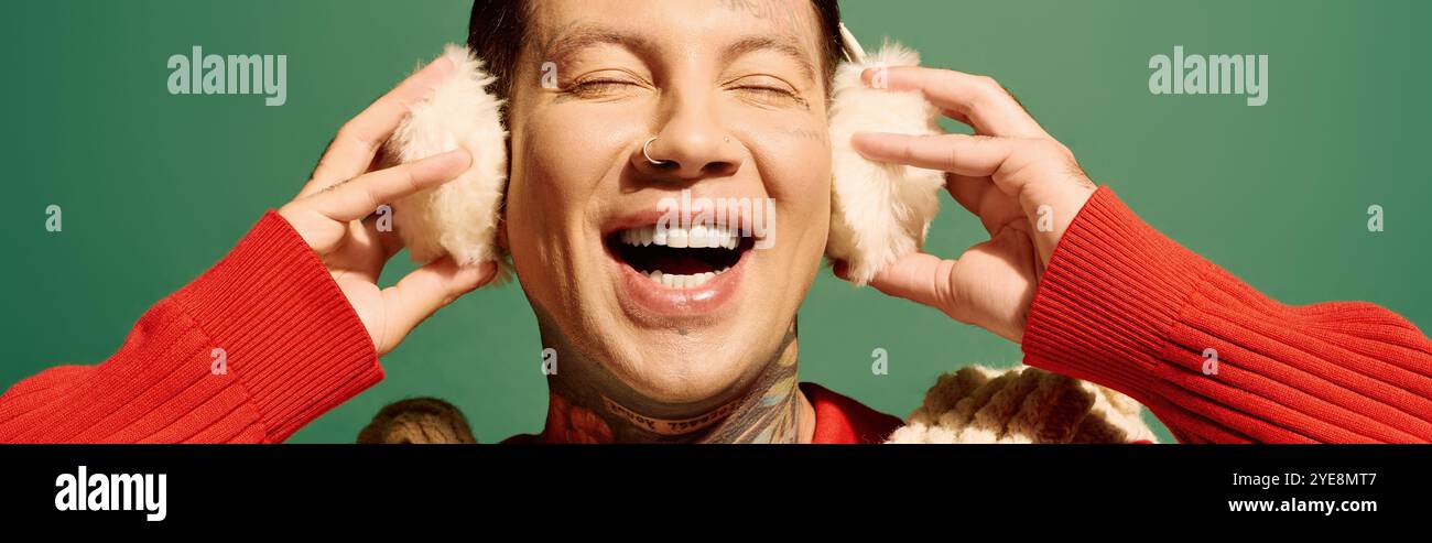 This cheerful young man smiles broadly while covering his ears with ...