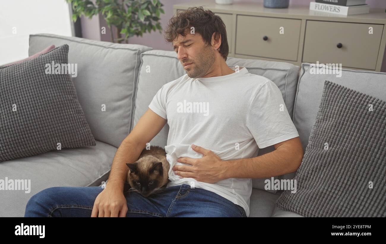 A young hispanic man experiencing stomach pain sits on a living room ...