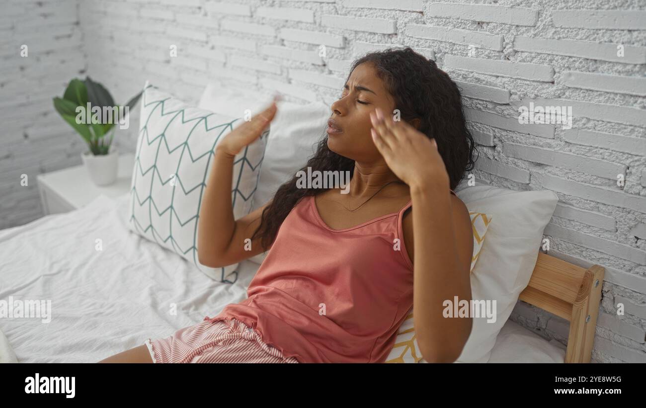 Woman fanning herself with hands lying on bed in bedroom with white ...