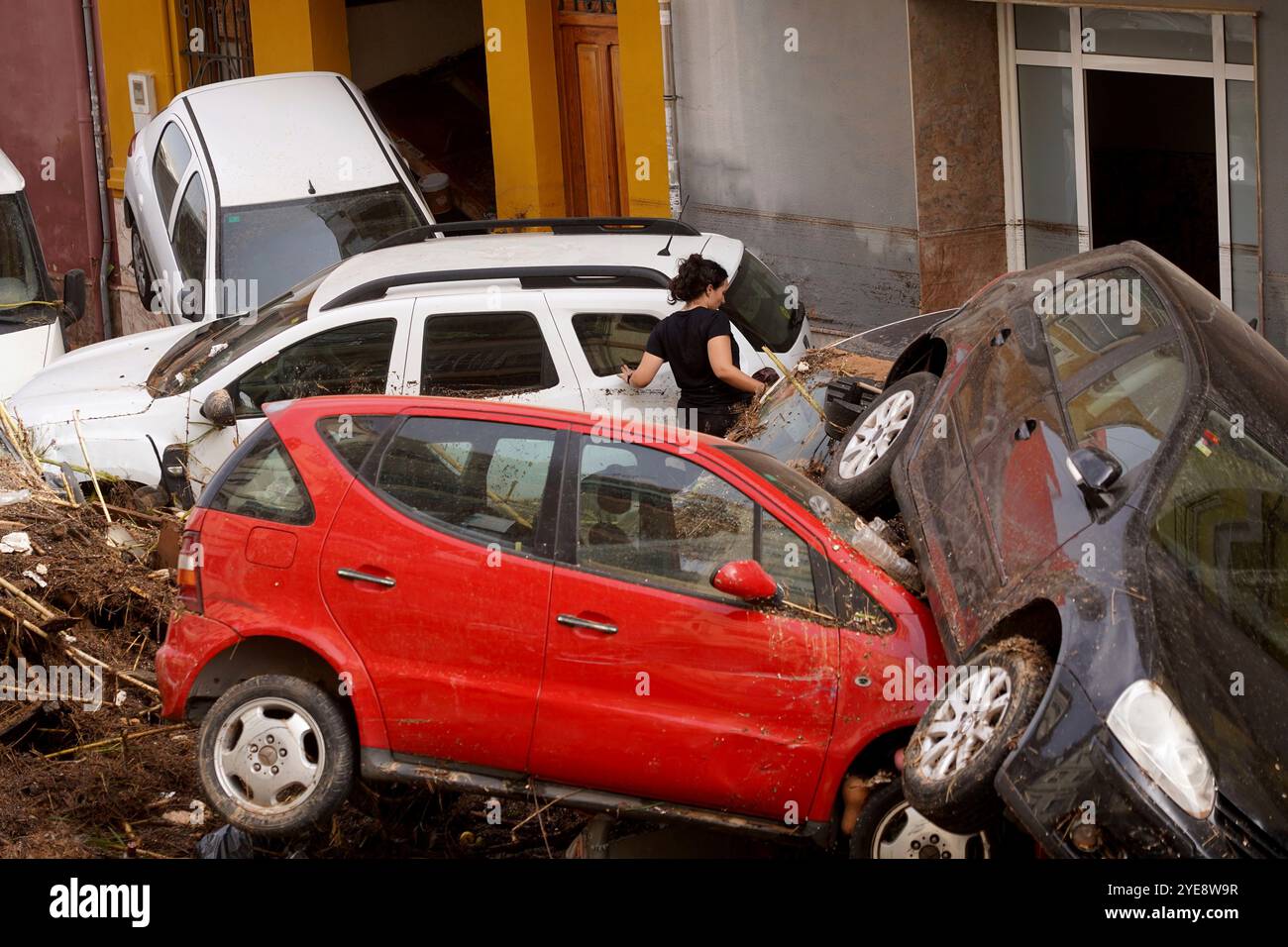 A woman walks through cars piled up after being swept away by floods in ...
