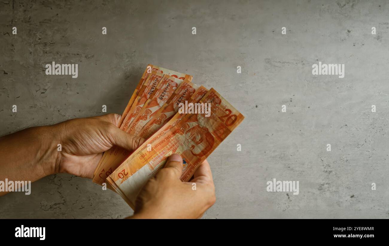 Hands holding philippine pesos against a concrete background ...