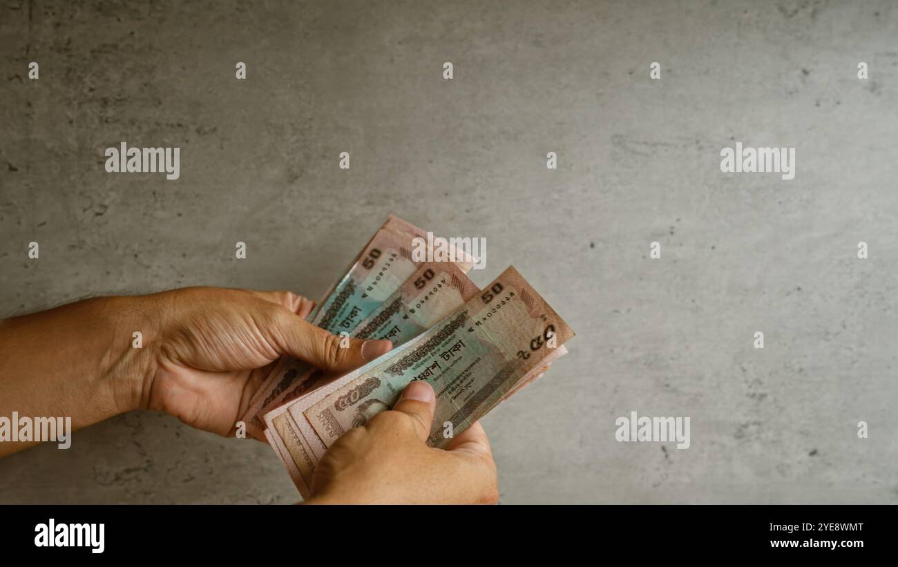 Man counting bangladesh taka with hands against a concrete backdrop ...