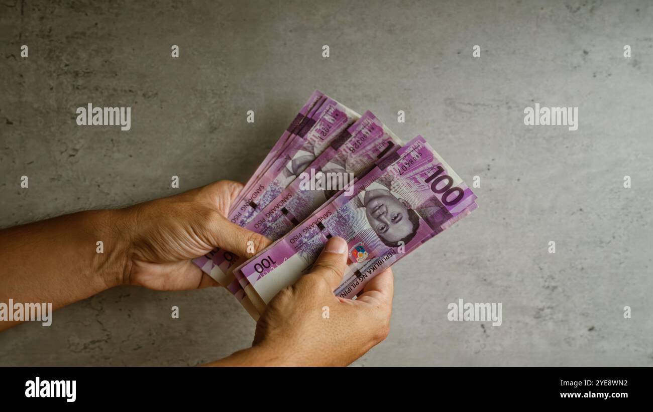 Man holding multiple philippine peso bills against a concrete ...