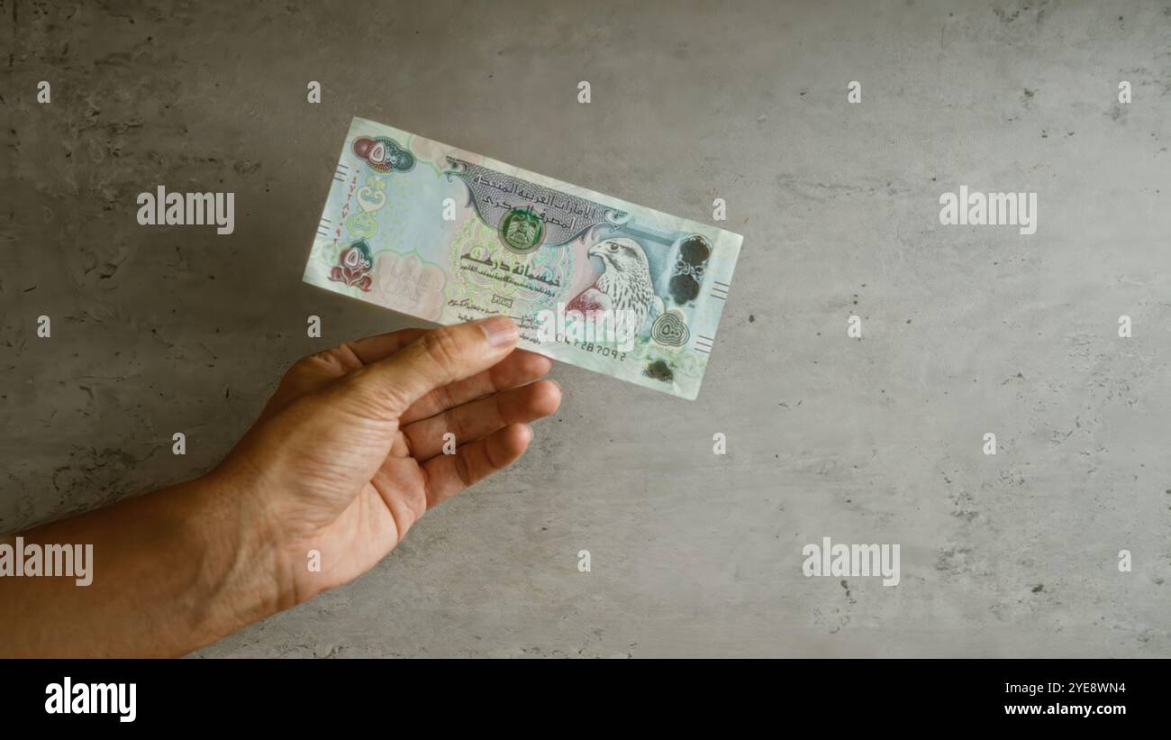 Hand holding a united arab emirates dirham banknote against a concrete ...