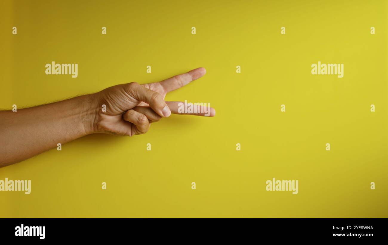 Hand showing victory sign against a bright yellow background with clear ...