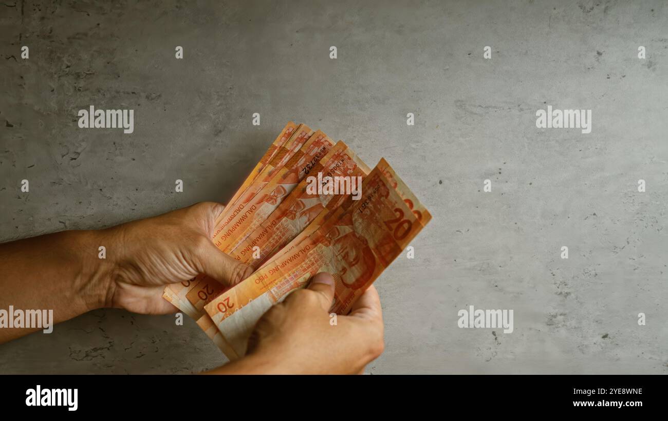 Hands holding multiple philippine pesos against a concrete background ...