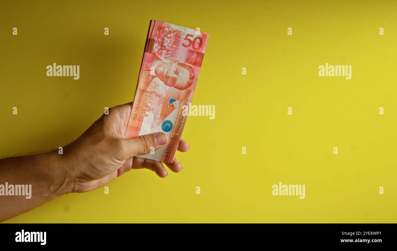 Hand holding philippine pesos against a yellow background, showcasing ...