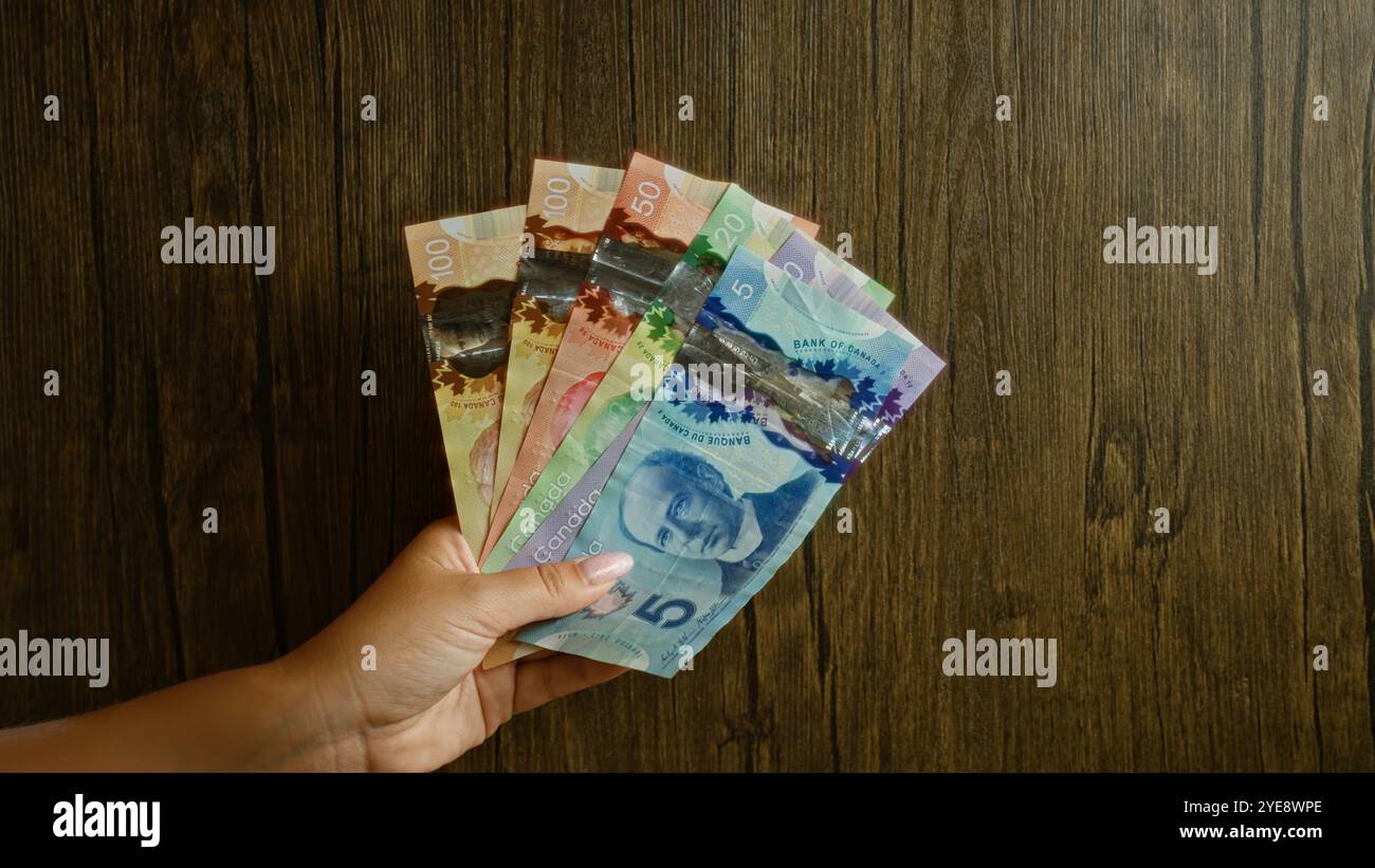 Hand holding canadian dollar bills on a wooden background, displaying ...