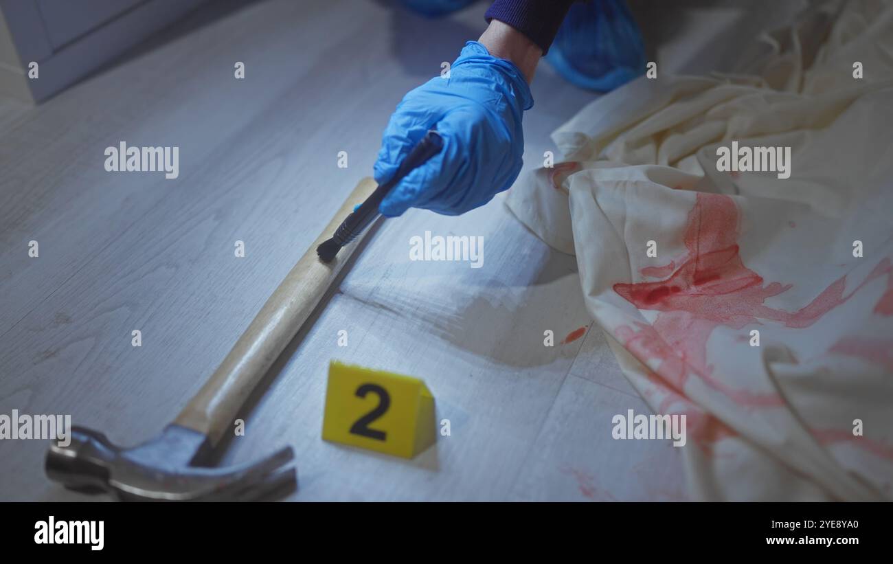 A man's gloved hand examines a hammer at a bloody indoor crime scene ...
