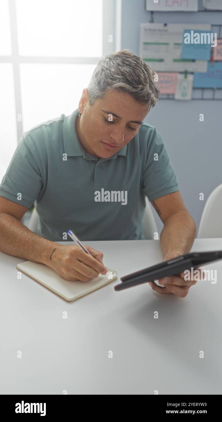 Young man taking notes while using a tablet in a bright office interior ...