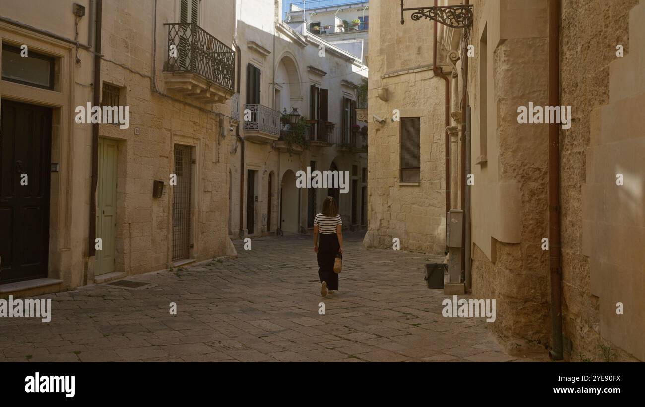 A young hispanic woman strolls through a historic stone alley in lecce ...