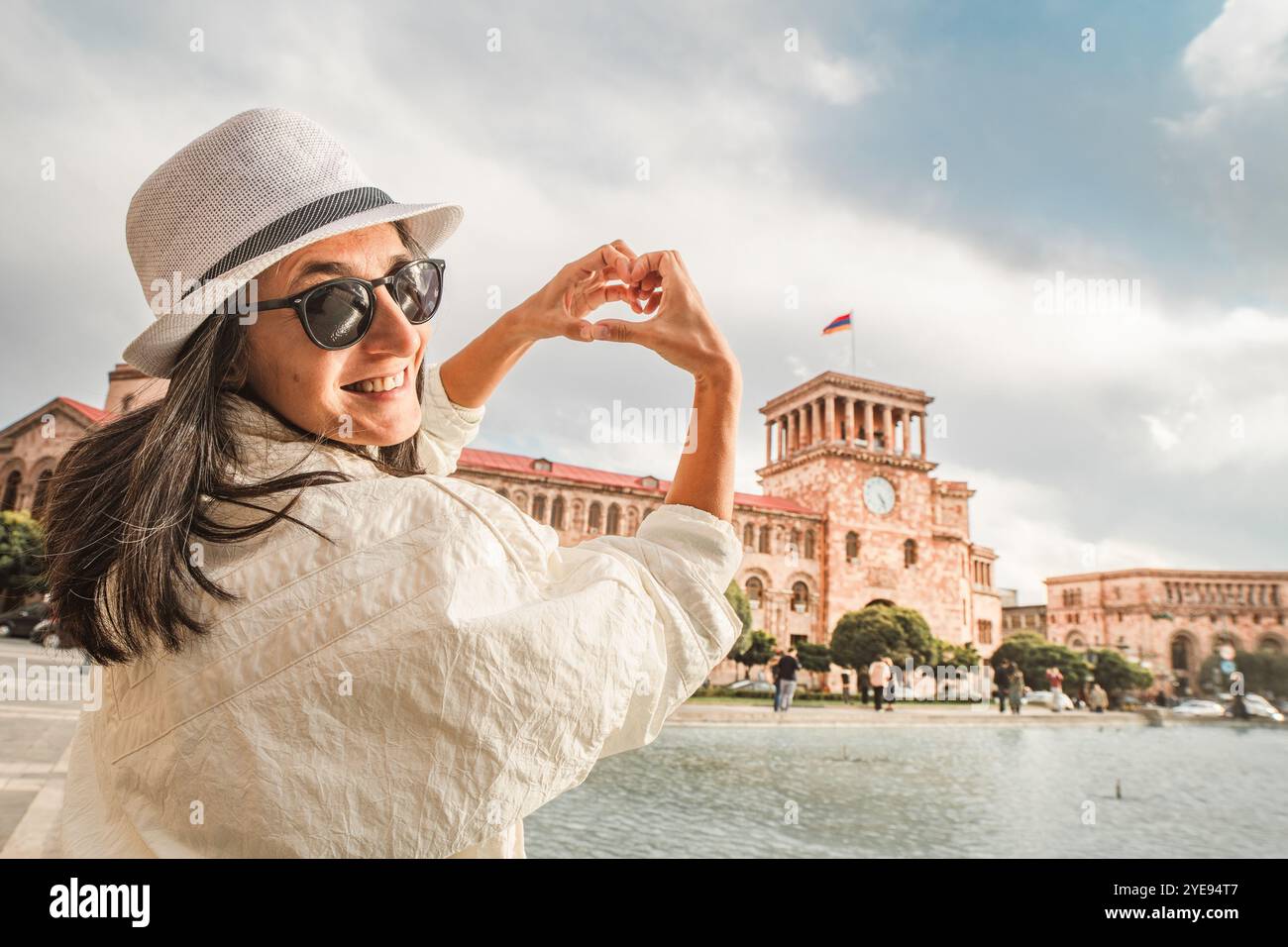 Young female tourist stand by fountain, making heart shape with hands ...