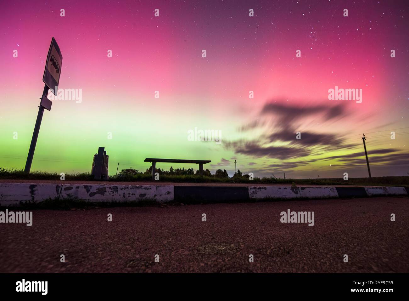 A bus stop under an aurora-filled sky, with vibrant green and pink ...