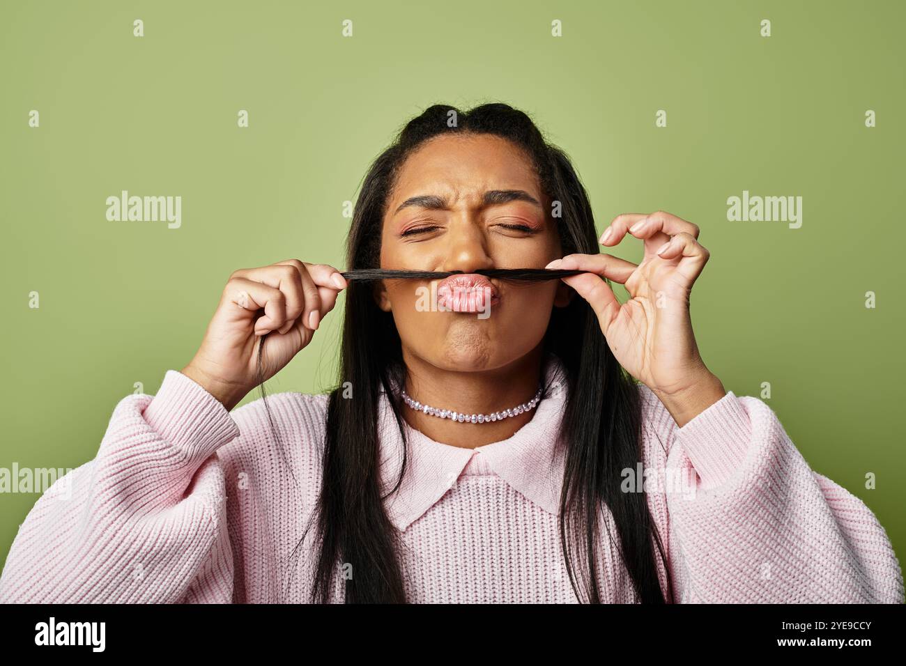 A young woman in warm attire is having fun, pulling her hair and making ...