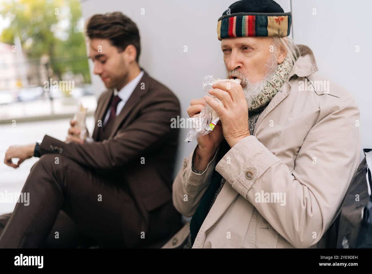 Hungry young entrepreneur and elderly homeless man eating together ...