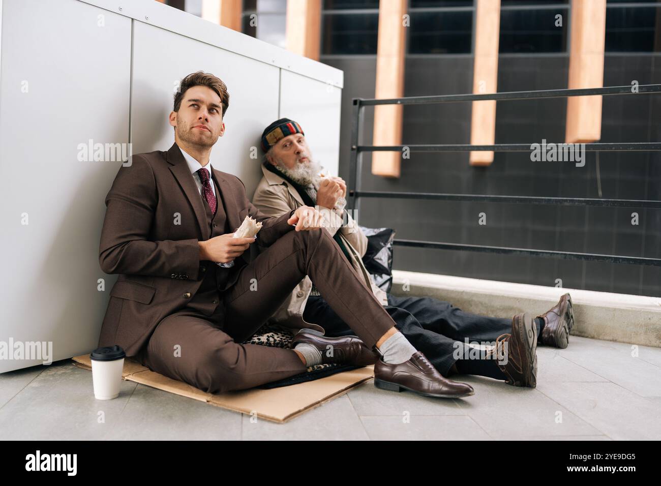 Pensive businessman wearing suit and tie sharing sandwich with elderly ...