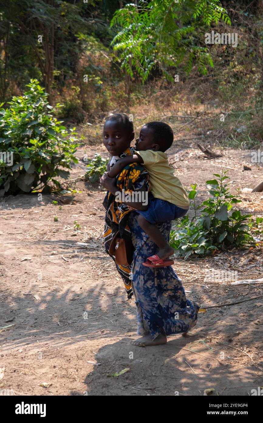 Young girl carrying her brother on her back in a village near Lake ...