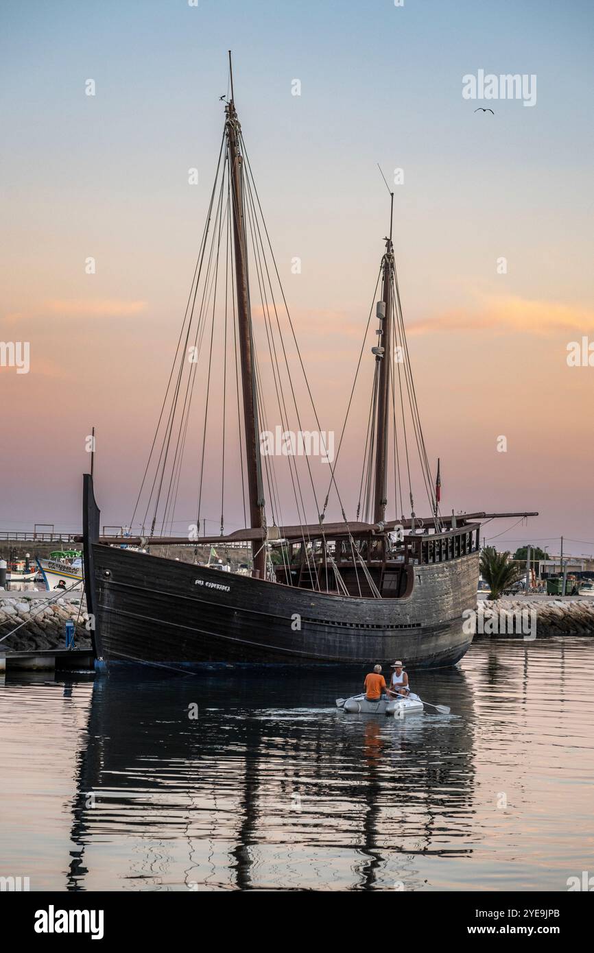 Two people rowing in a small boat past a larg ship mooring in a ...