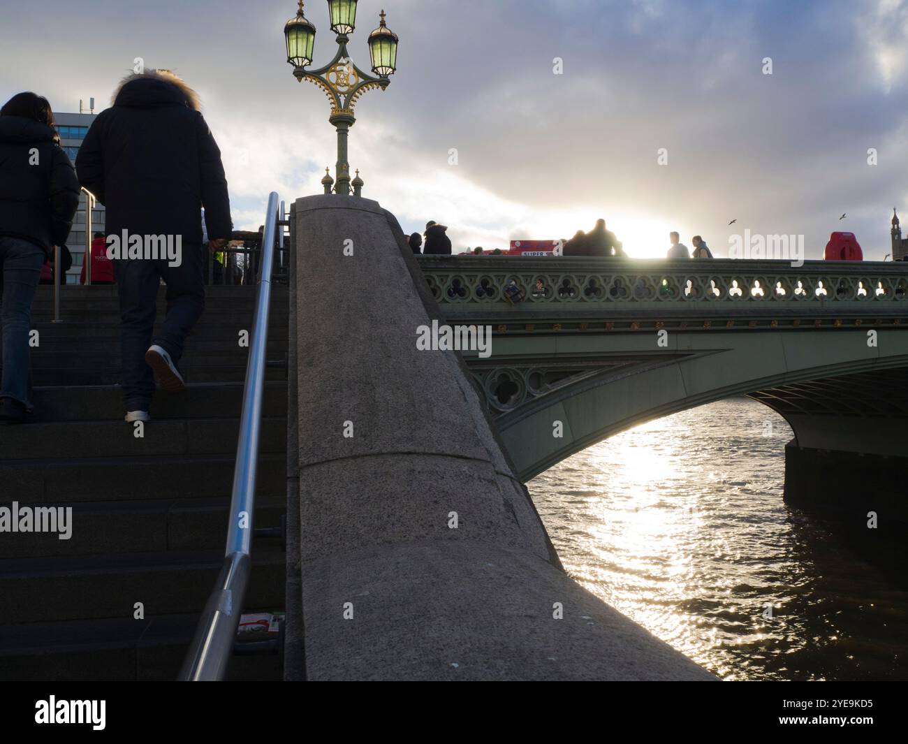 Backlit view of Westminster Bridge from Thames path with lit lamppost ...