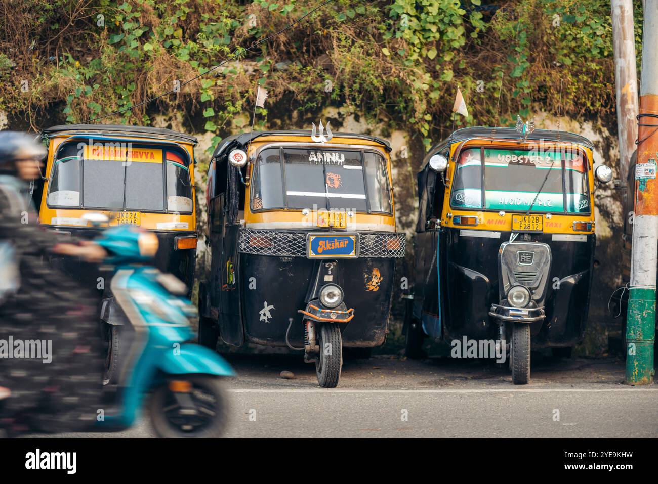 Auto rickshaws parked in a row along a street with a woman riding by on ...