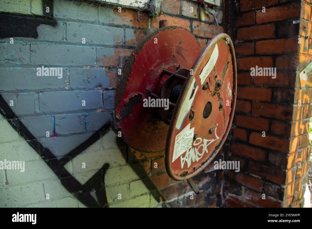 Rusted old red metal fire hose reel on the wall of an abandoned factory ...