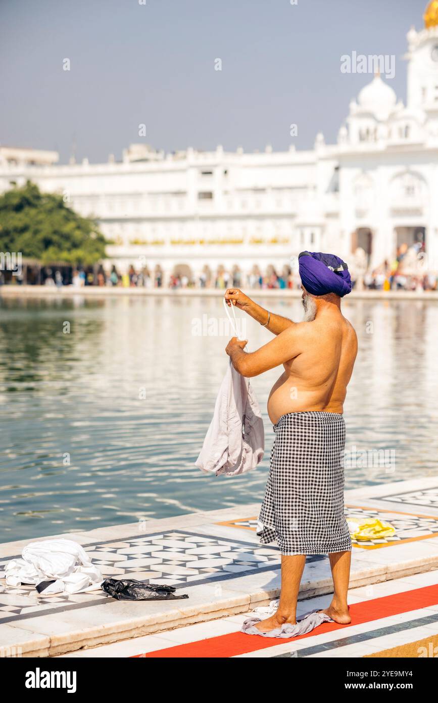 Golden Temple, a Sikh Gurdwara in Amritsar, Punjab, India, with a Sikh man standing shirtless on ...