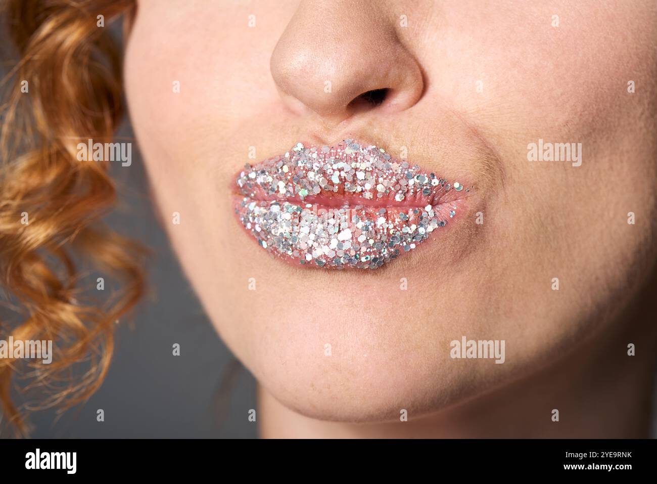 A young woman carefully adorns her lips with sparkling glitter for a ...