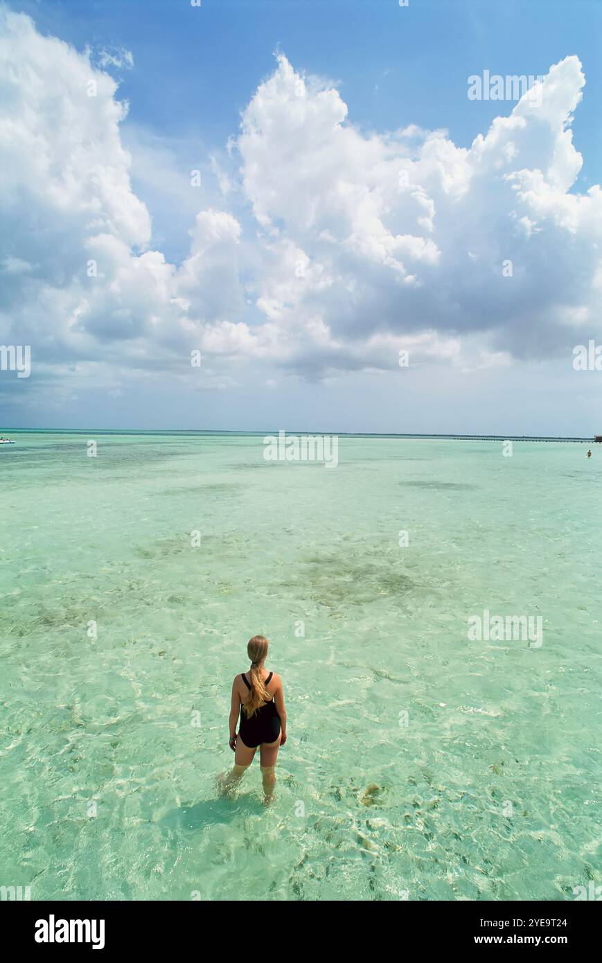 Young woman stands knee-deep in clear ocean water at a tropical holiday ...