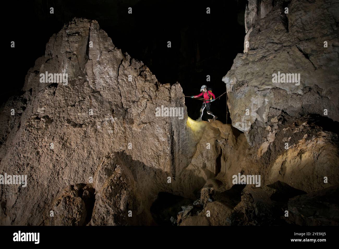 Female caver traverses the dangerous rock formations in a cave with her ...
