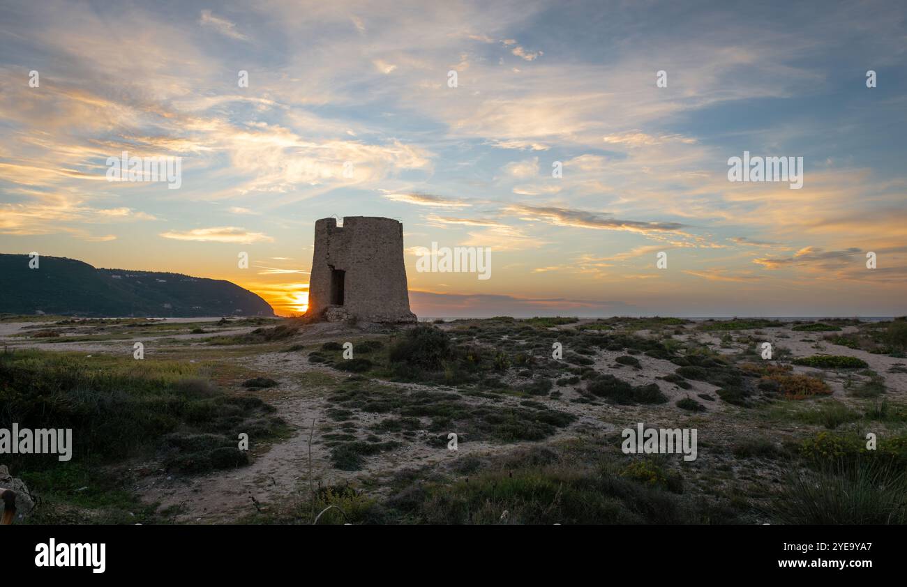 An old stone windmill on a beach at sunset with stunning sunlight and ...