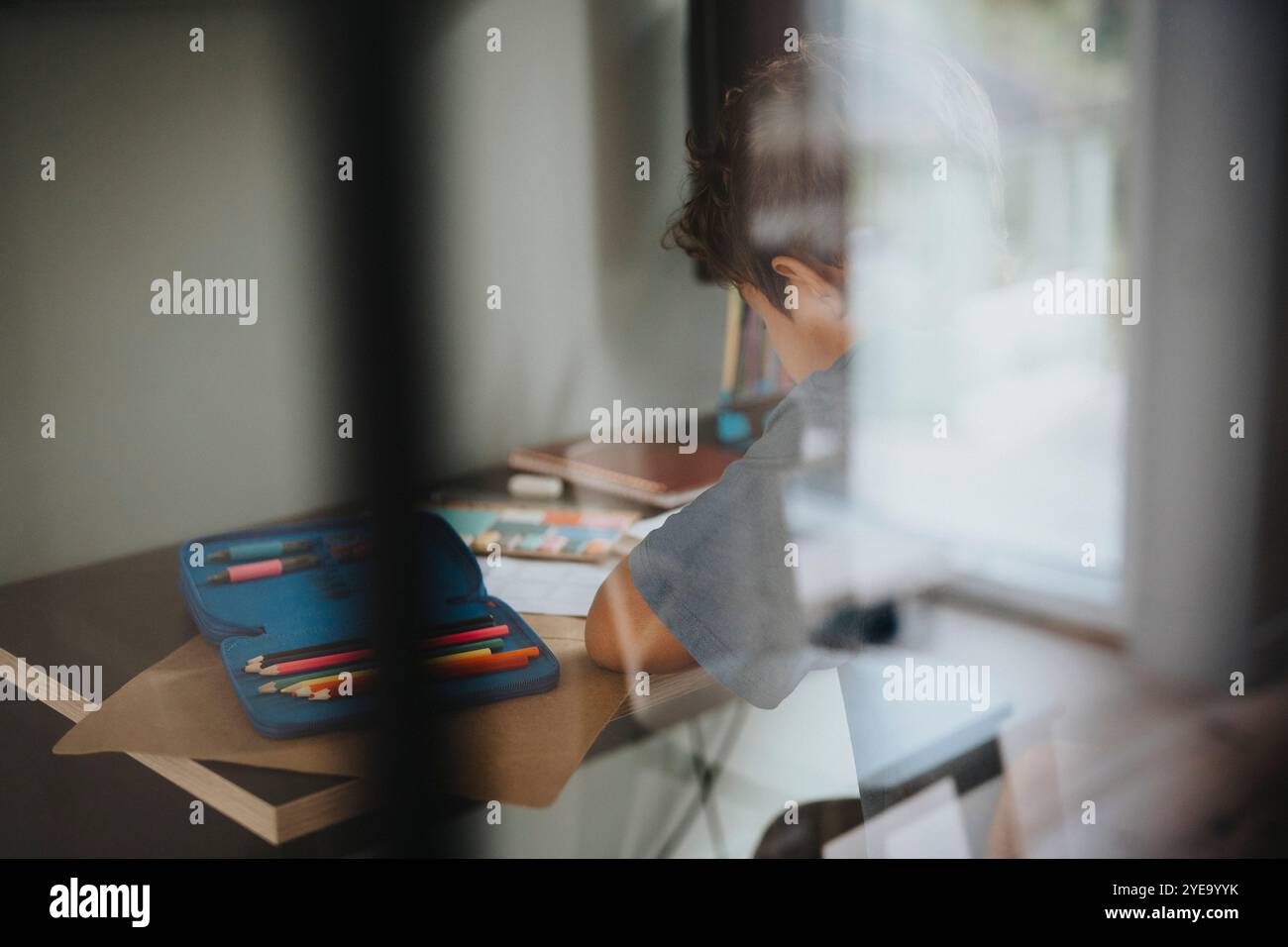 Rear view of boy doing homework seen through glass wall Stock Photo - Alamy