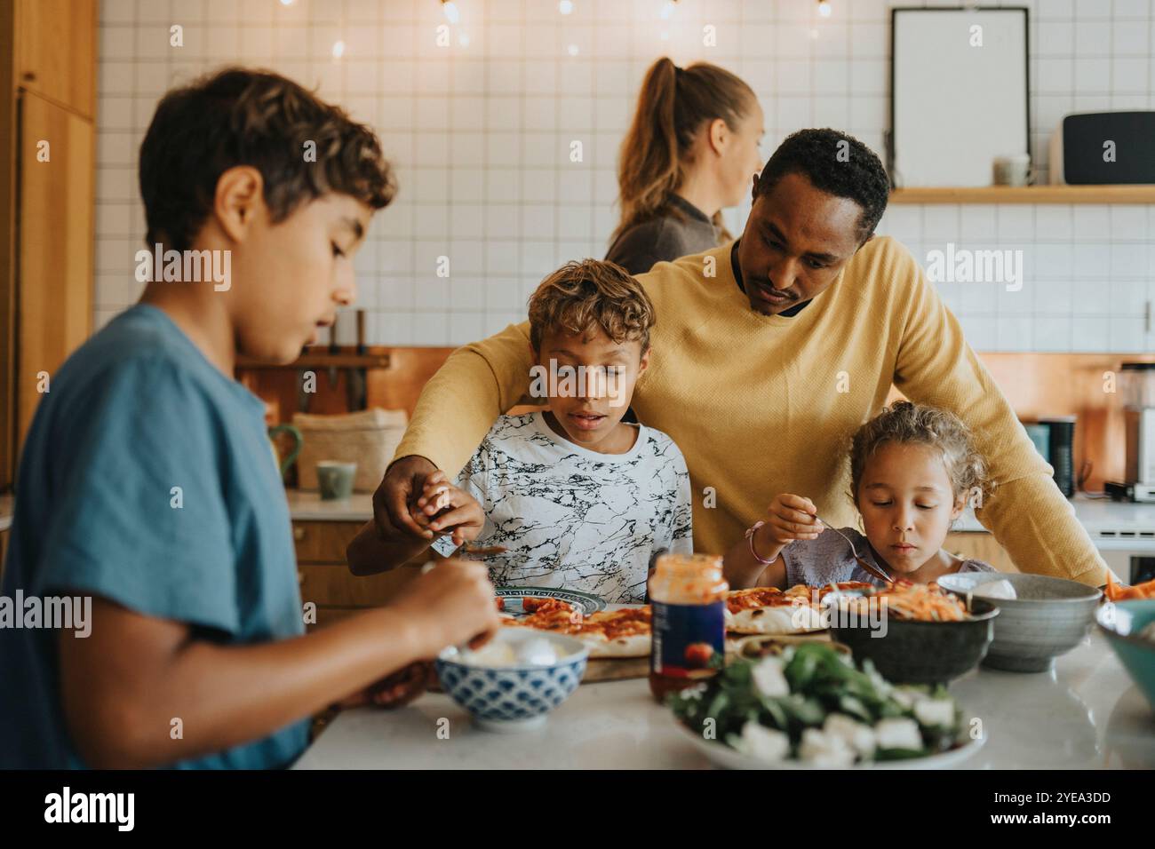 Father helping children making pizza while standing in kitchen at home ...