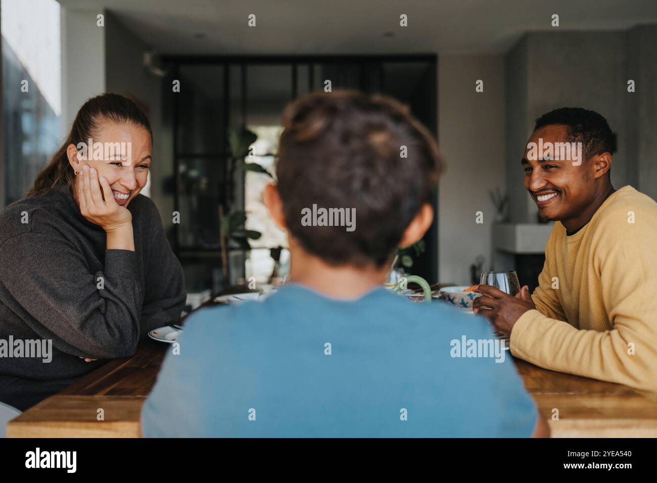 Happy parents talking with son at lunch while sitting near dining table ...