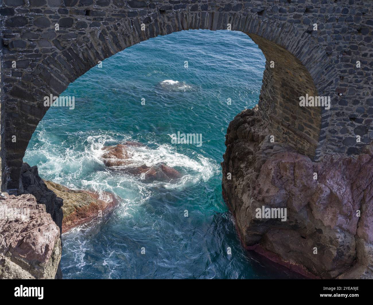 Surf splashing on the rocks under a stone archway at Ponta do Sol on ...