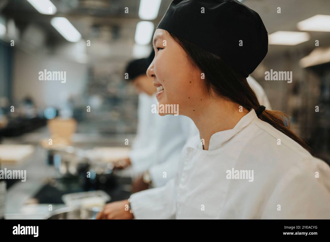 Side view of smiling teenage girl trainee wearing chef's hat in ...