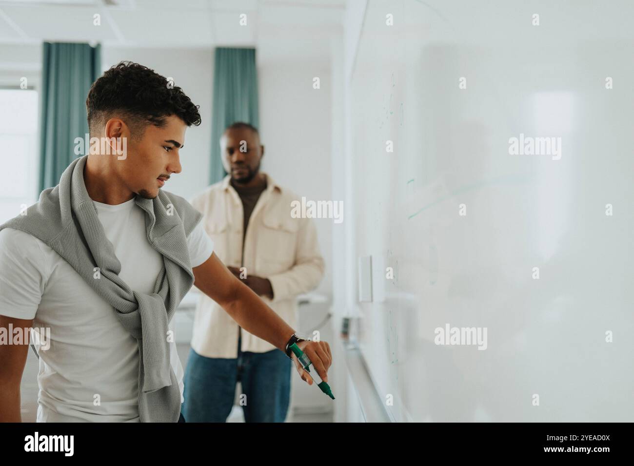 Teenage student with felt tip pen writing on whiteboard with teacher in ...