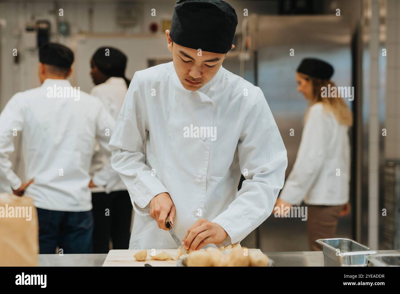 Male teenage trainee chopping food while practicing at restaurant high ...