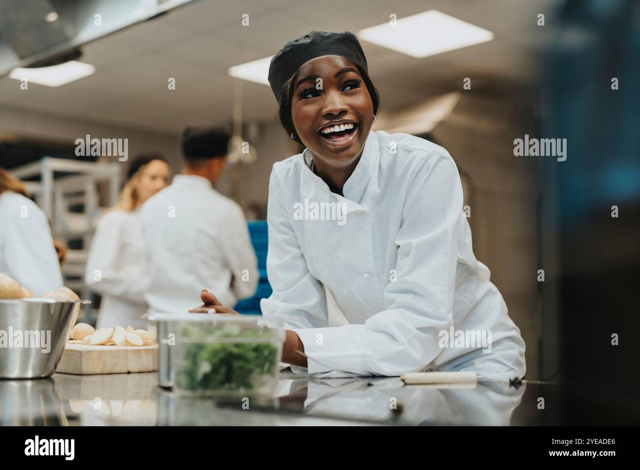 Cheerful female trainee leaning on kitchen counter Stock Photo - Alamy
