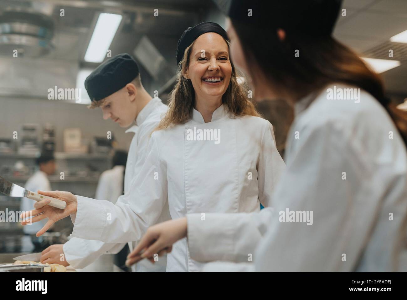Happy female teacher discussing with teenage trainee by male chef ...