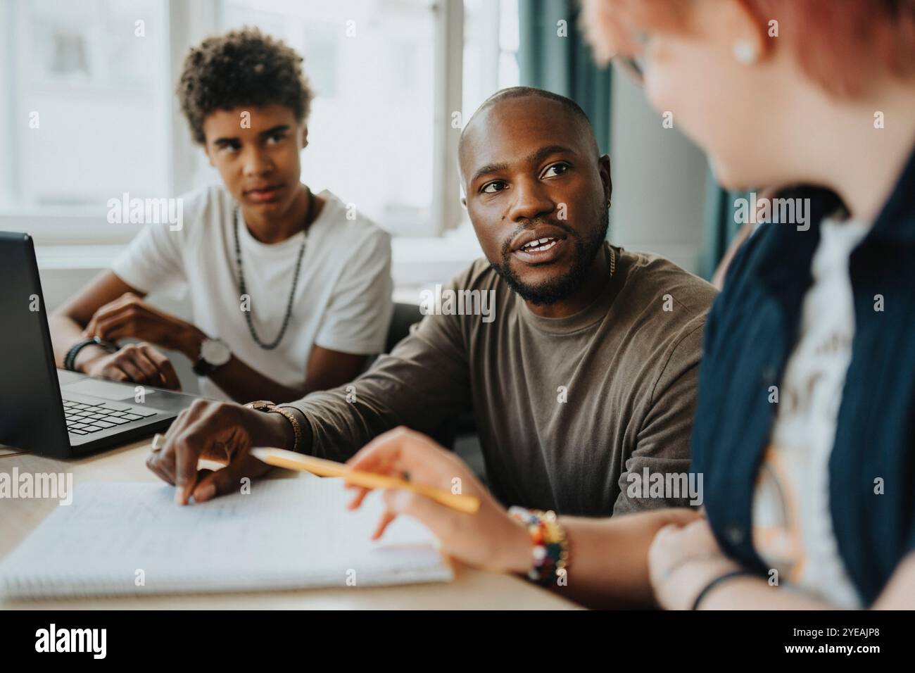 Male student looking at teacher discussing with non-binary person in ...