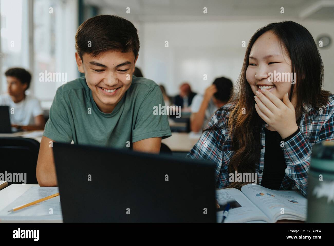 Happy teenage boy and girl using laptop while sitting together in ...