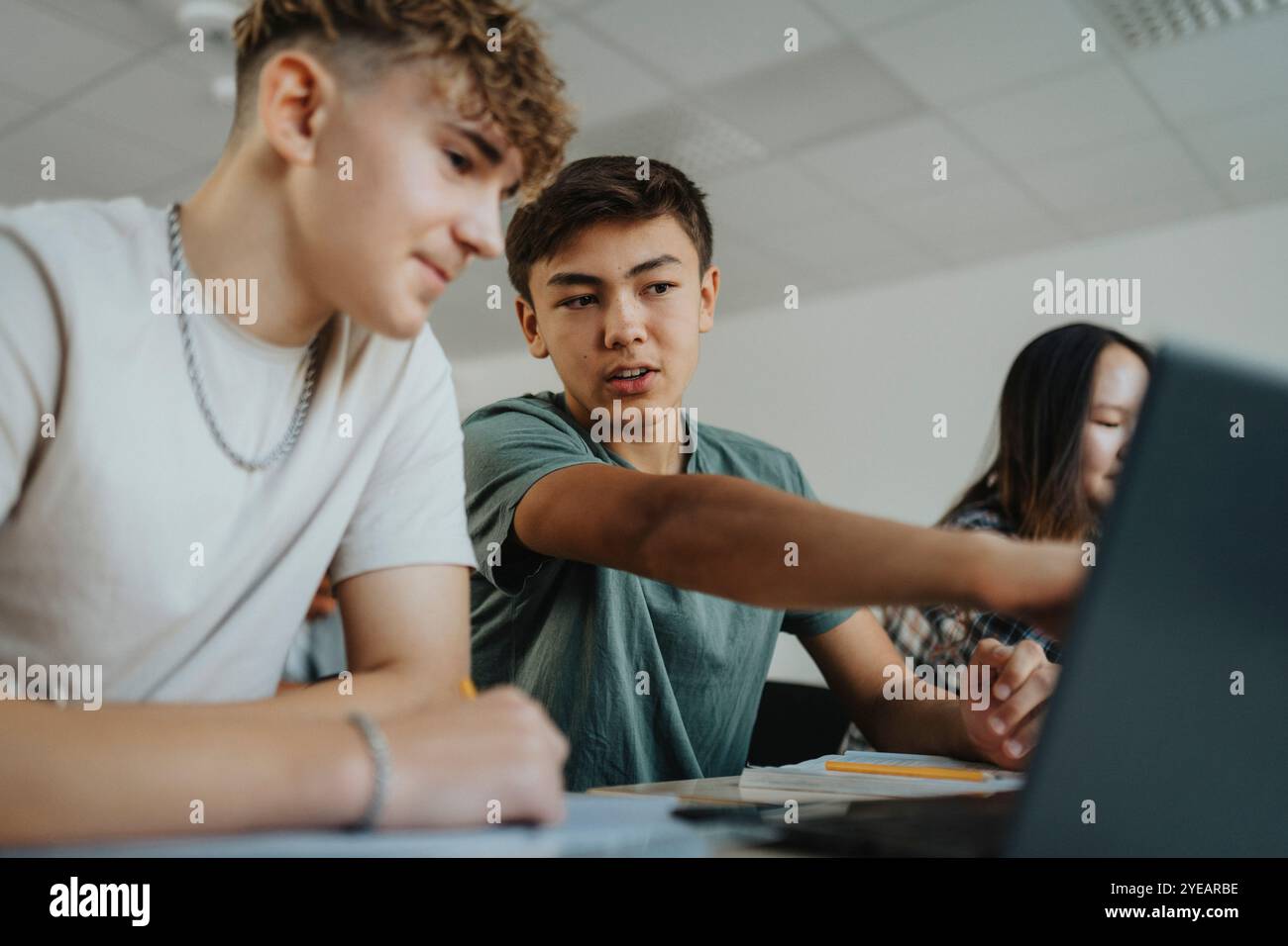 Male students discussing while using laptop in classroom Stock Photo ...