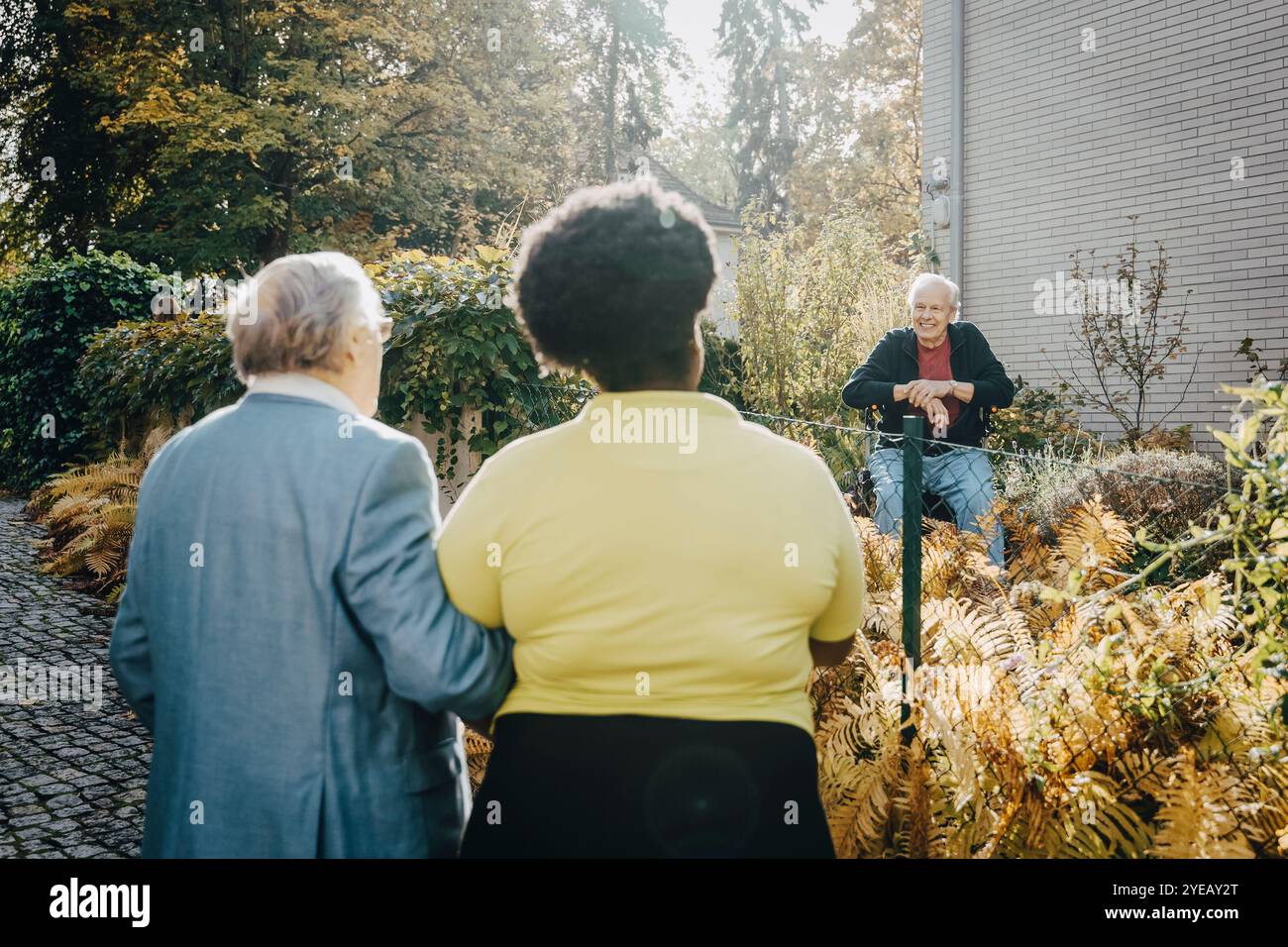 Rear view of caregiver and senior male talking with elderly man sitting ...