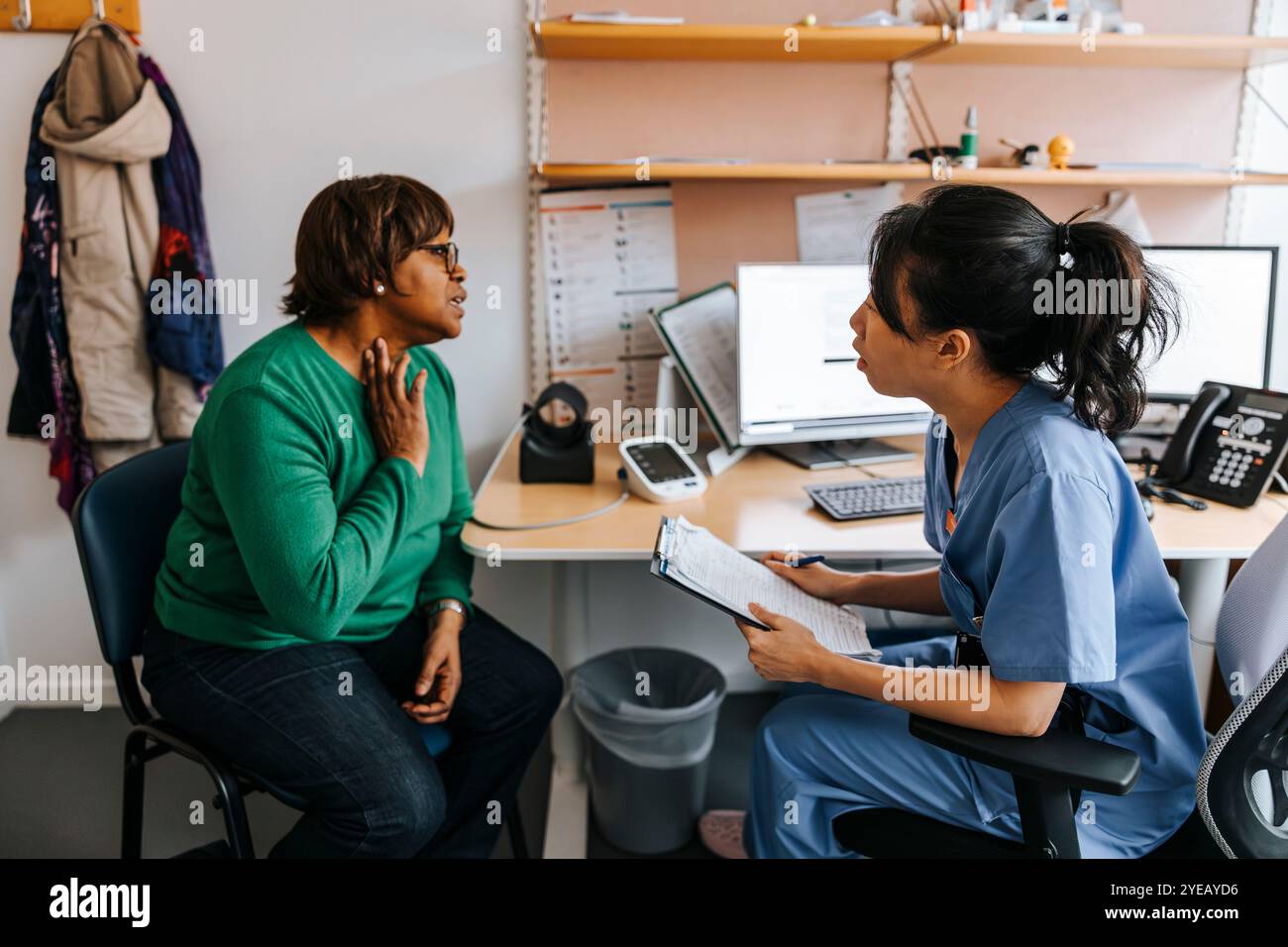 Senior woman showing neck problem to female doctor sitting on chair in ...