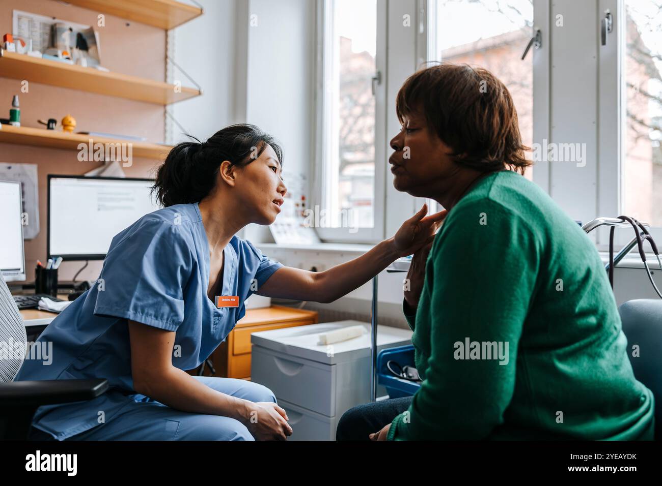 Female medical professional examining patient's neck while sitting in ...